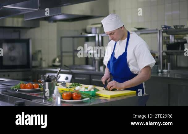 Caucasian cook slicing cucumber eating slice as chef passing at ...