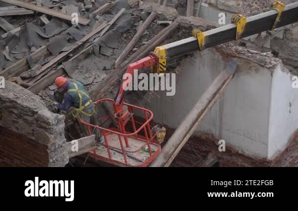 Demolition of old abandoned house, workman in orange helmet at crane basket destroy wooden roof ...