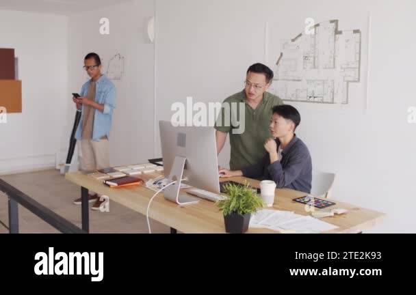 Dollying-in shot of team of four young Asian architects working ...