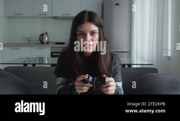 Beautiful excited young gamer girl sitting on a couch, playing and ...