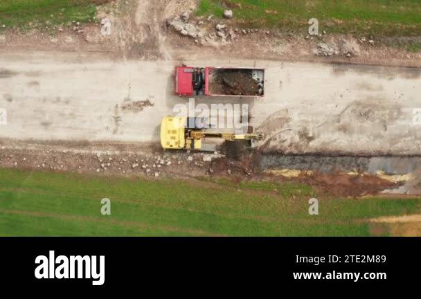 Top view of a yellow excavator loads soil from the field into a red ...