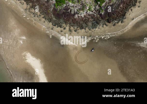 Footage of a car driving on the sand around rocks on a beach at low ...