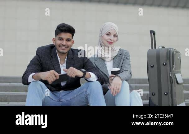 Two multiracial business people sitting at stairs with travel bag and ...