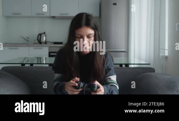 excited young gamer brunette girl sitting on a couch, playing and ...