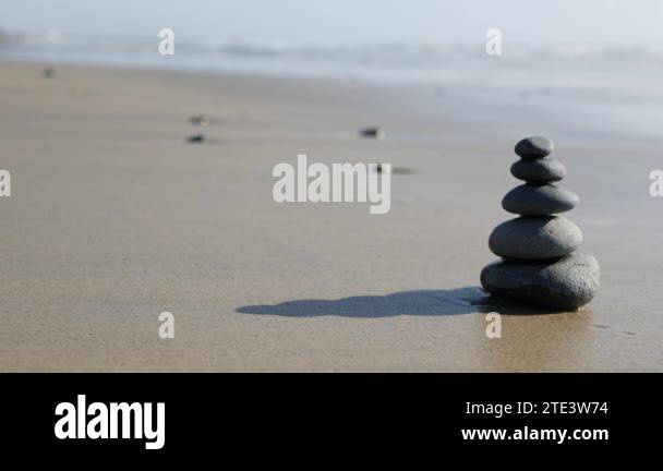 Rock balancing on ocean beach, stones stacking by sea water waves ...