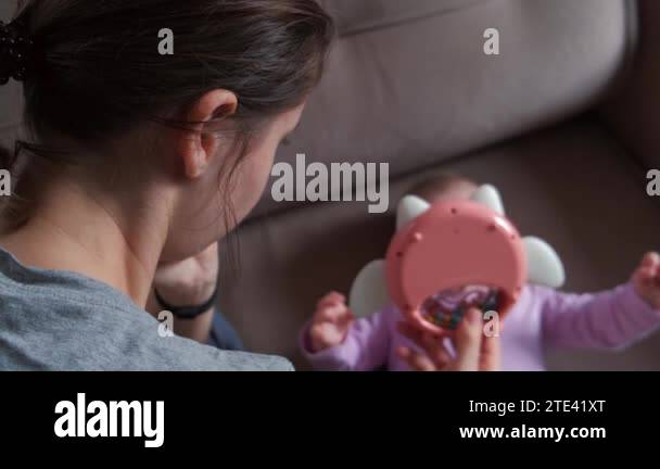 Back view of a mother playing with her little baby girl lying on a crib ...