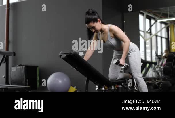 Female athlete doing dumbbell row exercise in gym indoors. Young woman ...