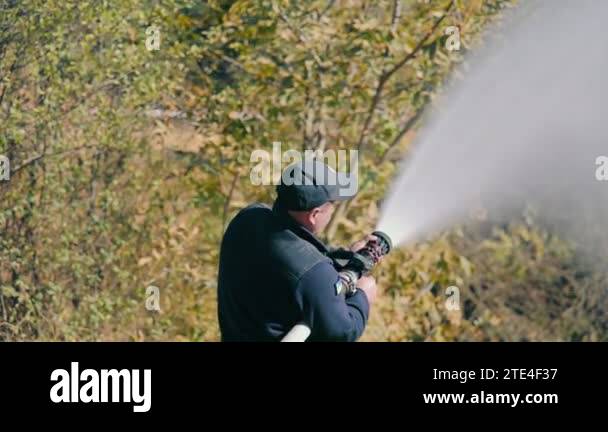 A man holds a fire hose and waters the object under high pressure. A ...