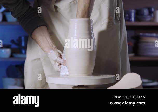 Male hands of potter form a soft white clay pot using pottery tools ...