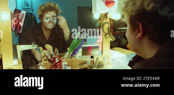 Male actor sitting in front of mirror and applying clown makeup with ...