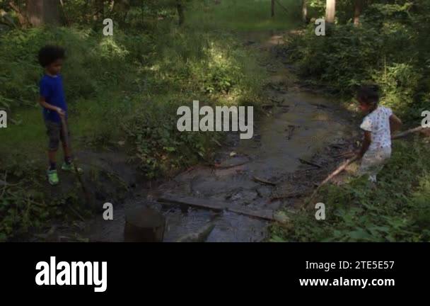 Two children play with sticks by forest stream. Benefits of nature play ...