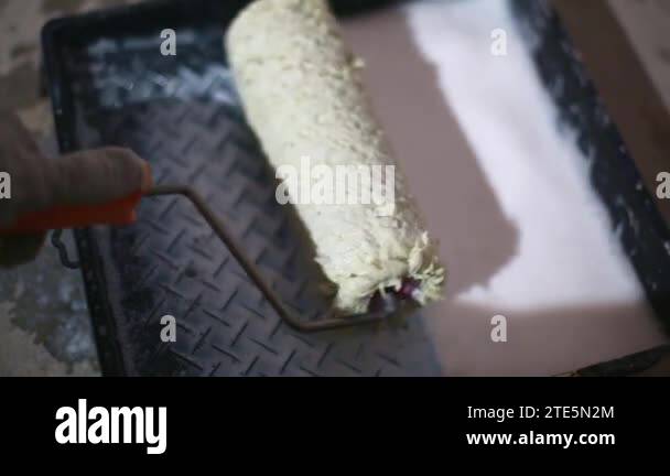 Applying a primer from the tray to the roller, evenly wetting and ...