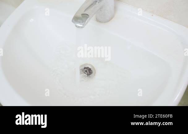 Water flows from the tap into the white sink, the hand changes cold ...