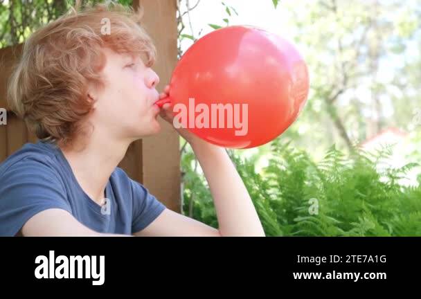 Teenager boy is blowing air balloon. Handsome redhead boy inflating red ...