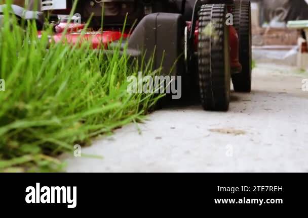 Garden red lawnmower. Low angle of side view of worker mowing lawn ...