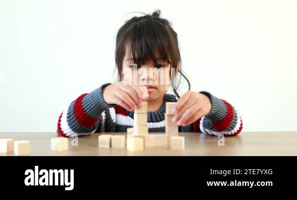 The little girl playing with wooden building blocks Jenga. Having fun ...