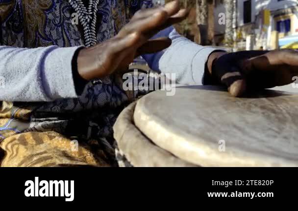 A Senegalese man plays a traditional djembe drum with his hands. West ...