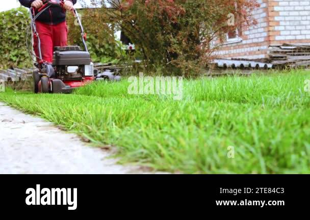 Garden red lawnmower. Low angle of side view of worker mowing lawn ...