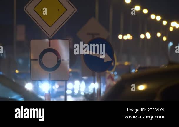 Roundabout road signs with blurred cars on city street traffic at night ...