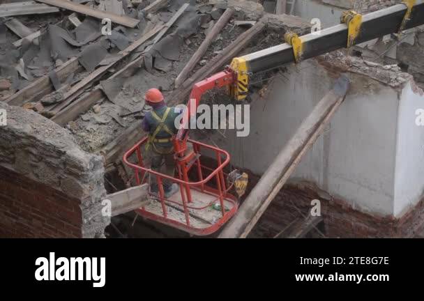 Demolition of old abandoned house, workman in orange helmet at crane basket destroy wooden roof ...