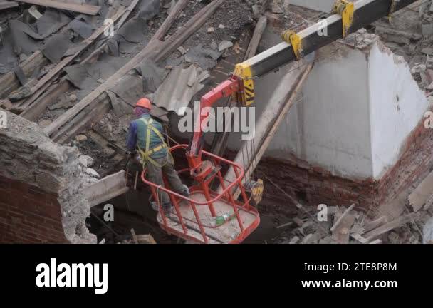 Demolition of old abandoned house, workman in orange helmet at crane basket destroy wooden roof ...
