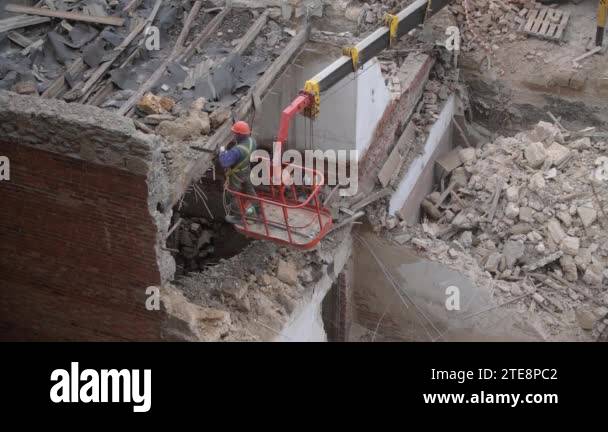 Demolition of old abandoned house, workman in orange helmet at crane basket destroy wooden roof ...