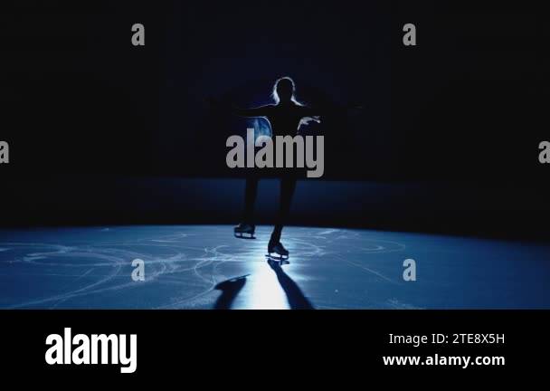 Young figure skating artist rotates on ice arena in dark against ...