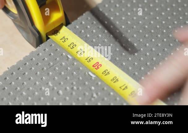 Measuring the dimensions of gray thick insulation foam using a yellow ...