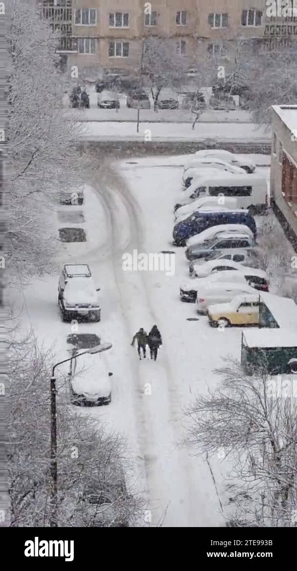 People walk on snowy street among houses and cars covered with snow ...