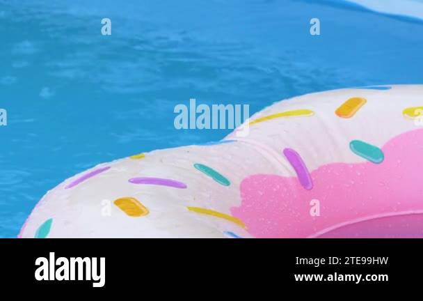 CLOSE UP: Rain begins pouring down on an inflatable donut floating ...