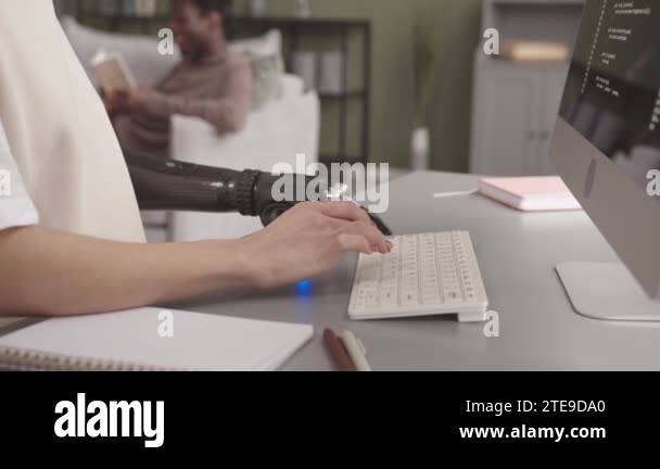 Slowmo shot of young attractive woman with bionic arm typing program ...