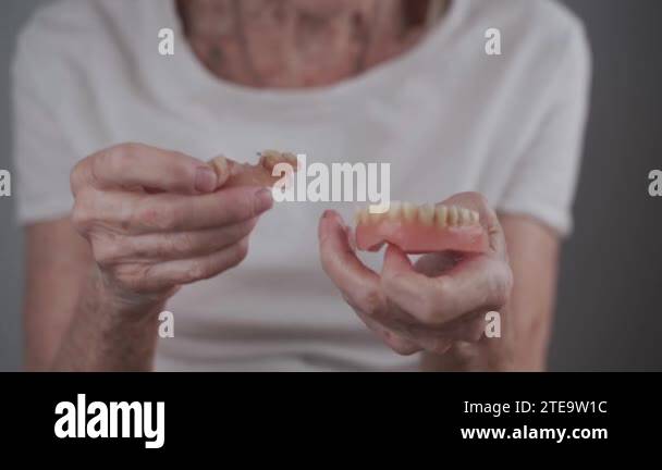 Senior woman holding close-up of dental prosthesis in hands. Old female ...