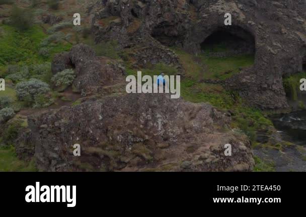 Orbit shot around hiker sitting and resting on narrow ridge above water ...