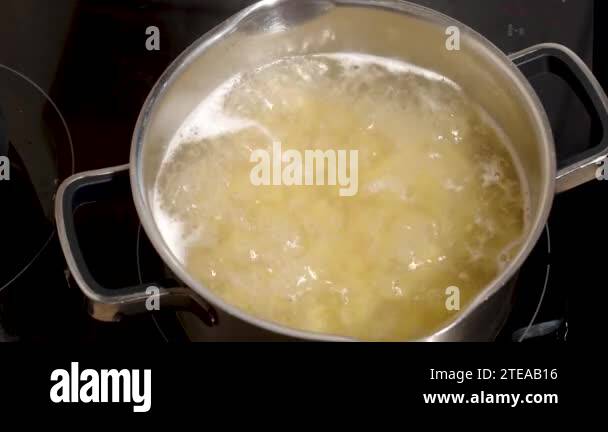 Hand stirring raw pasta boiling in boiling water in a metal pot on the ...