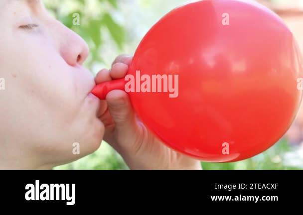 Teenager boy is blowing air balloon. Handsome redhead boy inflating red ...