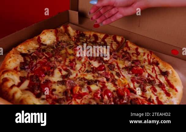 Appetizing large pizza in box on red background. Womans hand takes ...