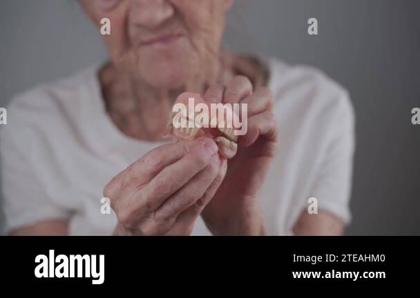 Toothless senior woman holds denture in her hands and makes a funny ...
