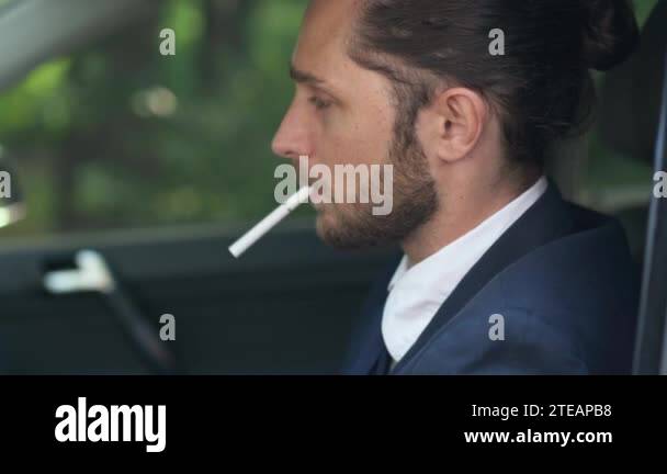 Close-up careless young man lightning cigarette sitting in car on ...