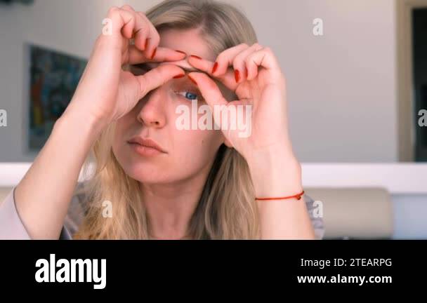 Ageing. Sagging skin. Young woman does facelift exercises by looking in ...