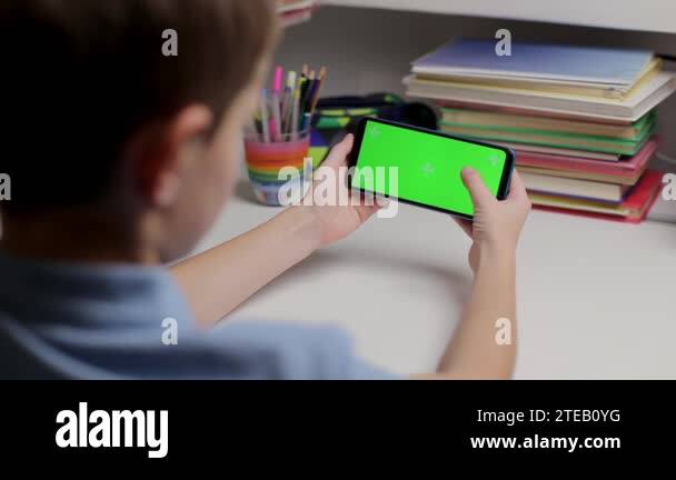 Boy holding a smartphone with a green screen at home, scrolling ...