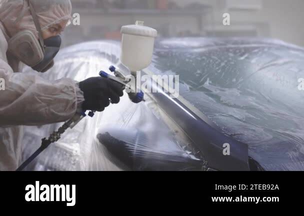 Painting vehicle parts at car service workshop. Male technician is air ...