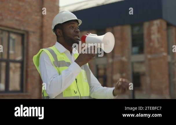 Expressive african american foreman in safety helmet shouting into ...