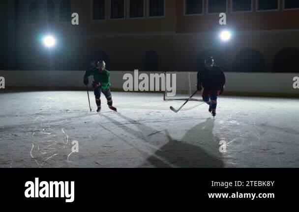 Two men in uniforms and helmets with hockey sticks skate on ice arena ...