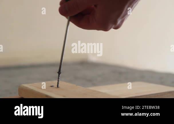 A mans hand is screwing a self-tapping screw into a board with a ...