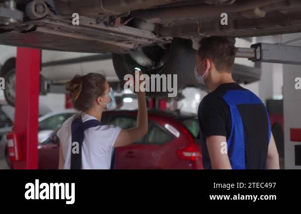Female mechanic inspecting car suspension. Strong woman coaching a male ...