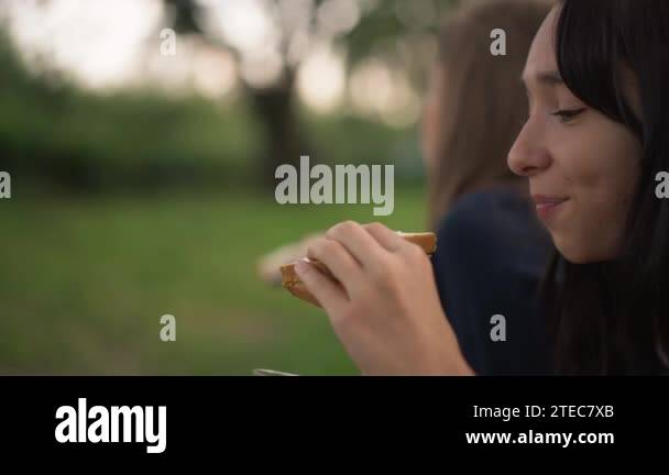 Side view teenage girl on the right eating sandwich with blurred friend ...