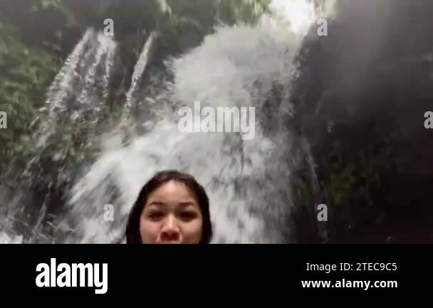 Live camera of a pretty girl swimming in river under waterfall. Happy ...