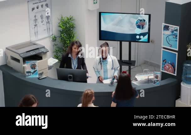 Secretary working at busy hospital reception desk to help patients with ...