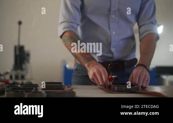 Leather craftsman works in a workshop. Master making leather products. Man carves leather sheet ...