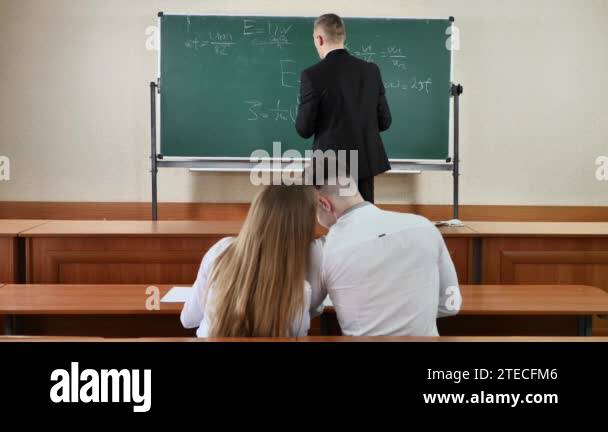 Teacher giving a lecture in a classroom and writing math formulas on ...